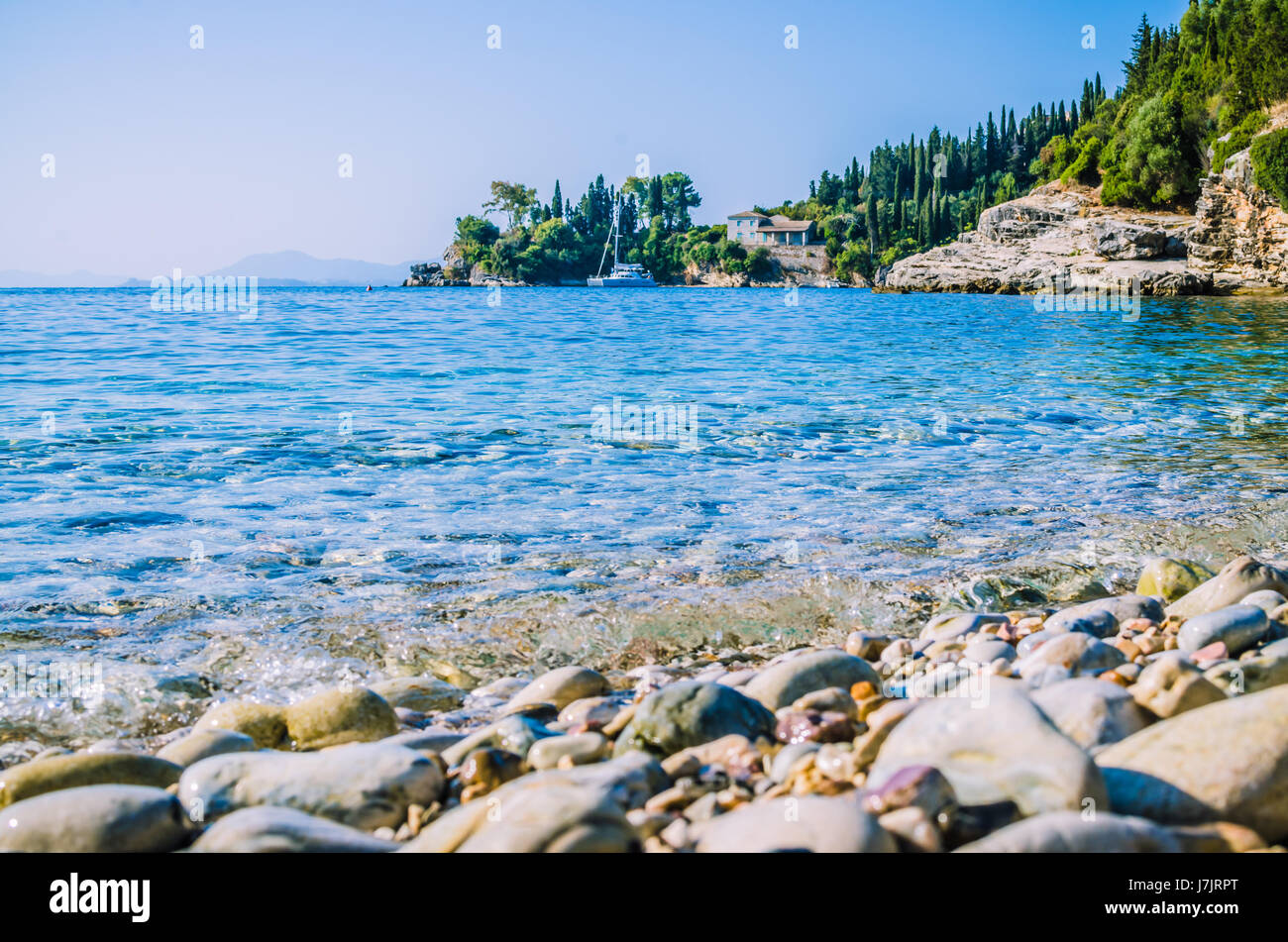 Pebble beach near Kalami with pine and cypress trees and an yacht at ...