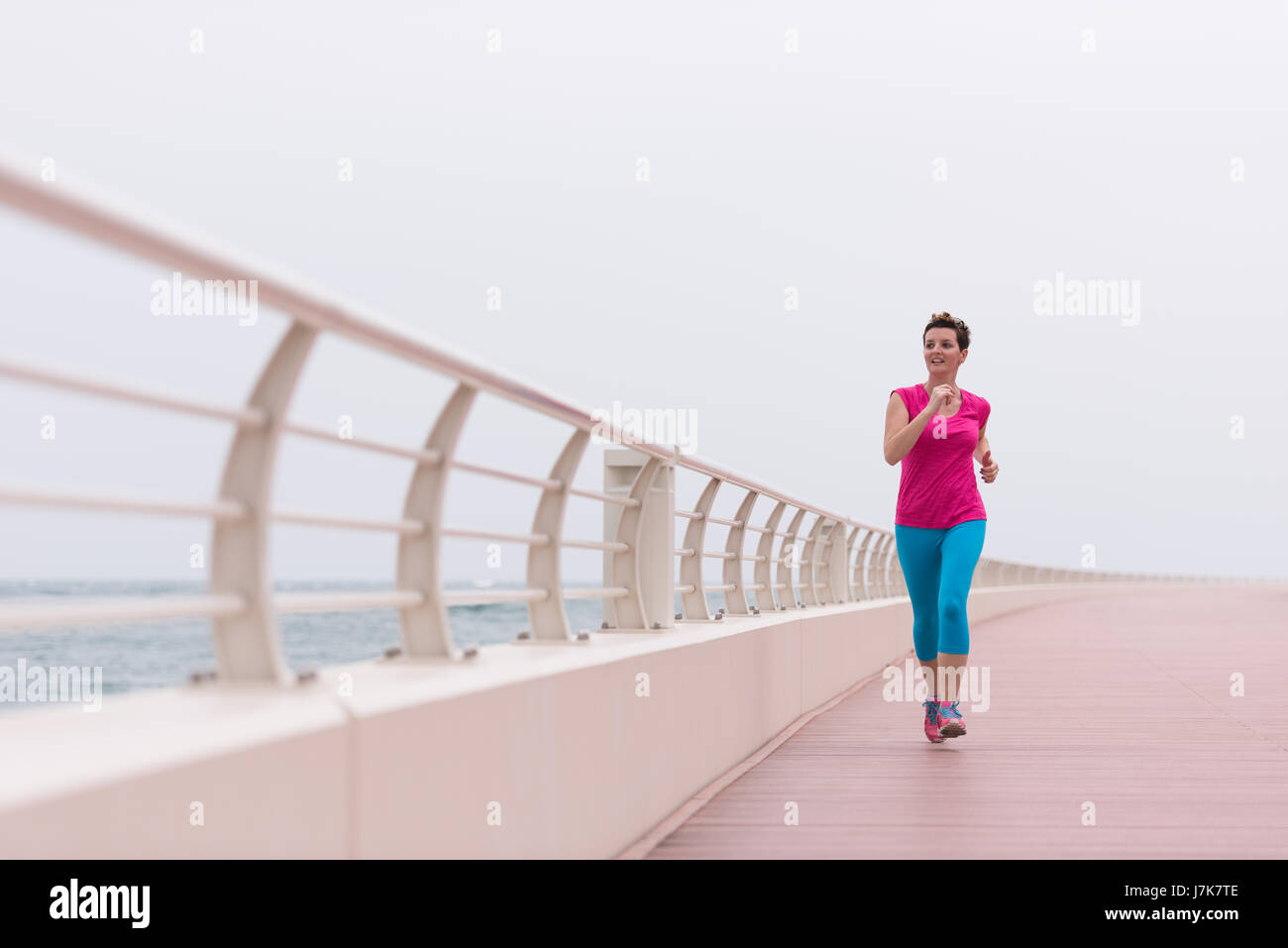 very active young beautiful woman busy running on the promenade along ...