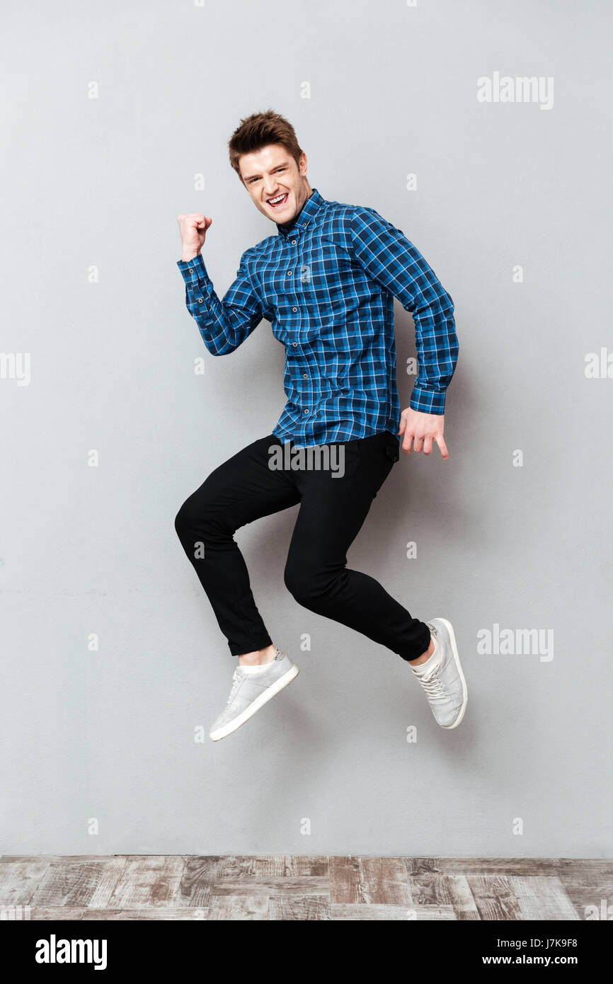 Picture of screaming young man standing over grey wall and jumping ...