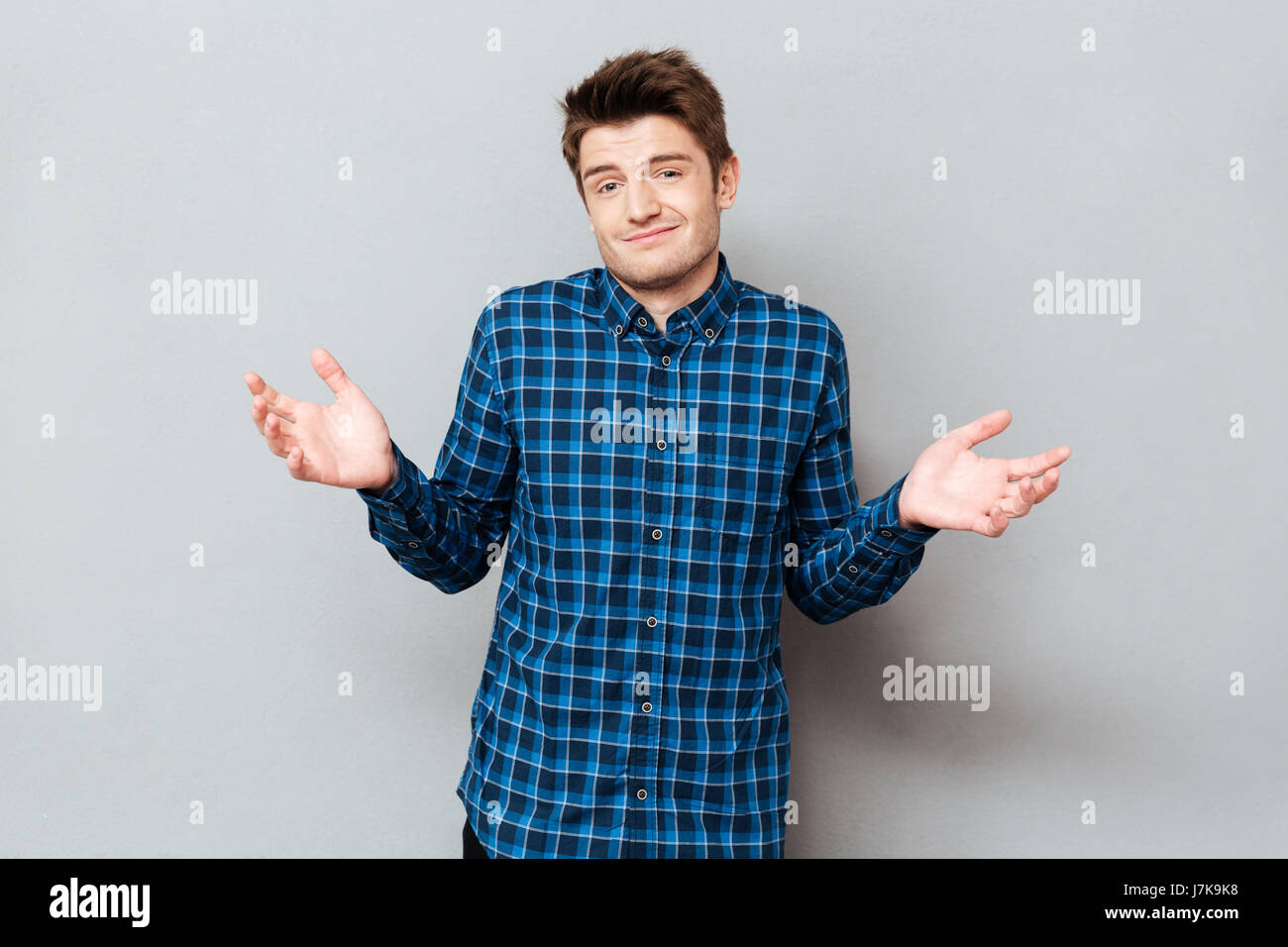 Image of confused young man standing over grey wall. Looking at camera ...
