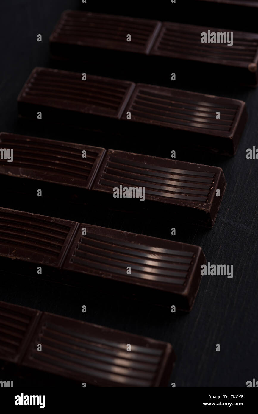 Close-up of dark chocolate bar tiles in a row over wooden background ...