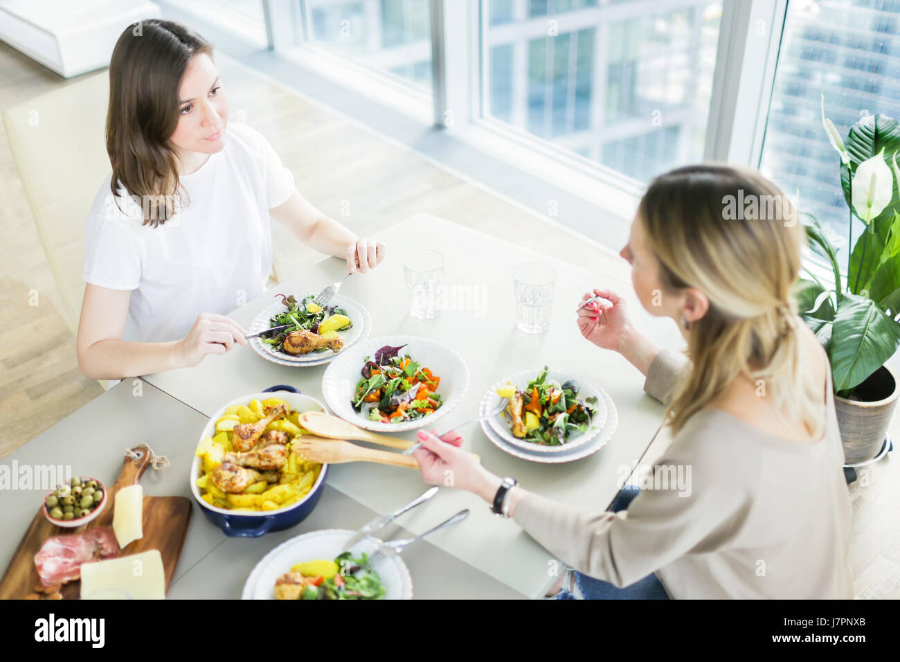 Young women eating together at the table in modern apartment. Top view ...