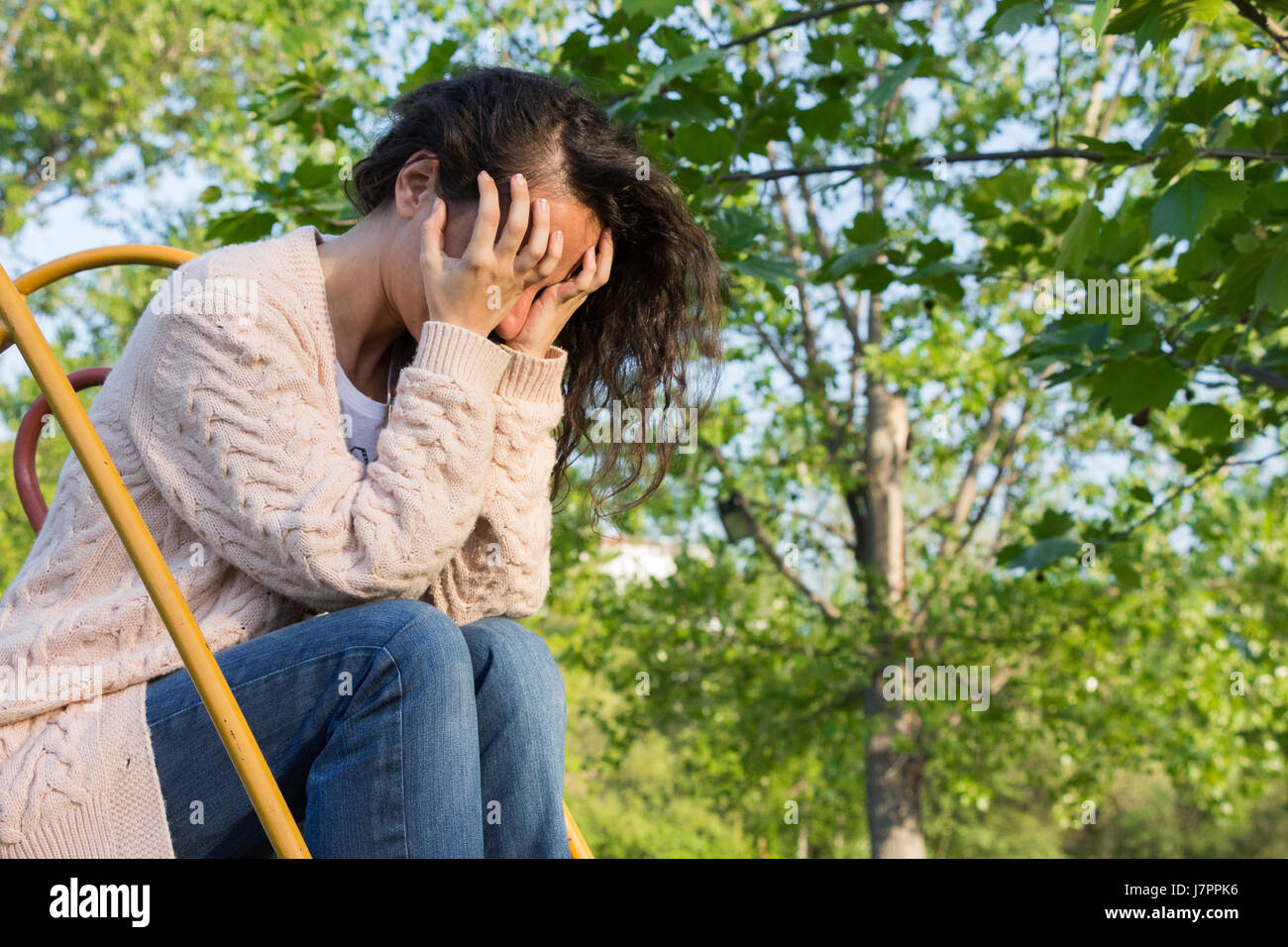 A young woman covering her face with both hands sitting on the top of a ...