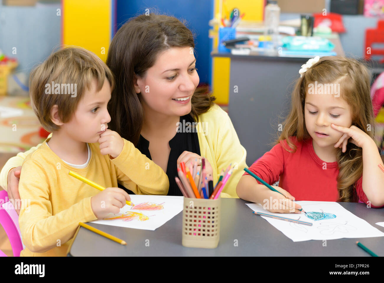 Kids drawing at kindergarten being supervised by educator Stock Photo ...