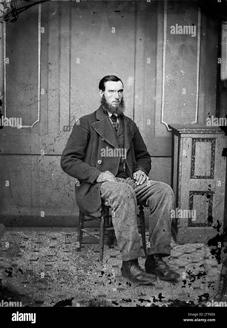 The image portrays a man sitting, captured in a relaxed or ...