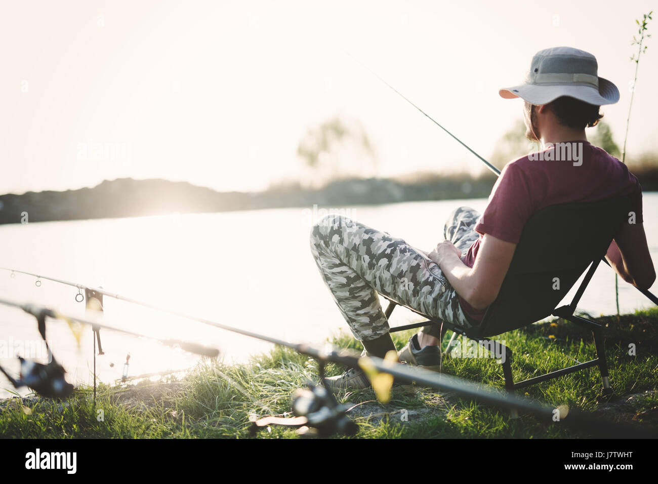 Young man fishing on lake at sunset enjoying hobby Stock Photo - Alamy