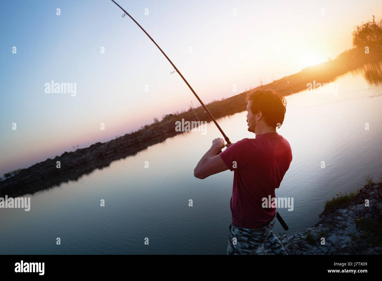 Young man fishing on lake at sunset enjoying hobby Stock Photo - Alamy