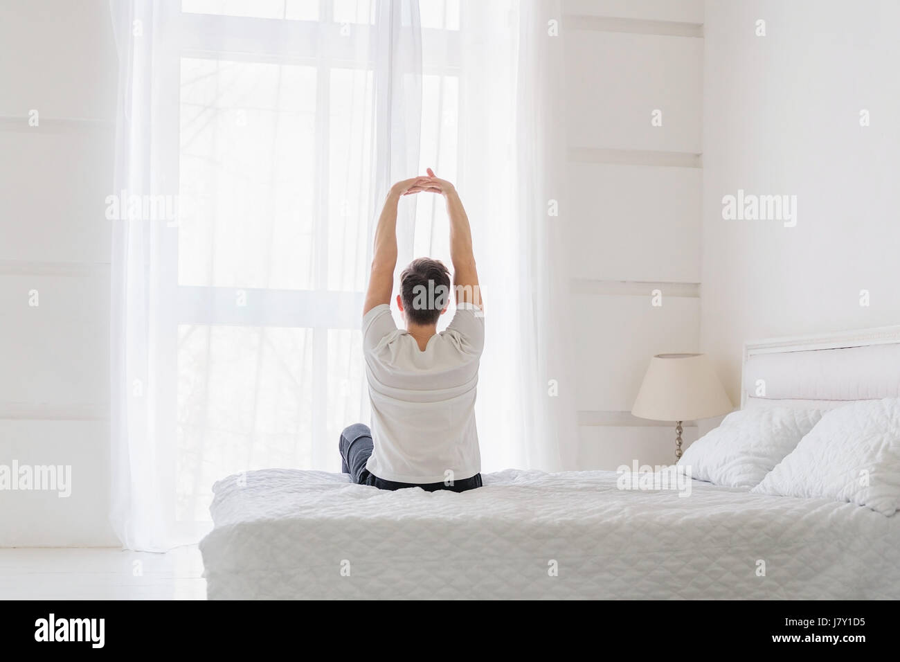 Young man sitting with hands raised up against window Stock Photo - Alamy
