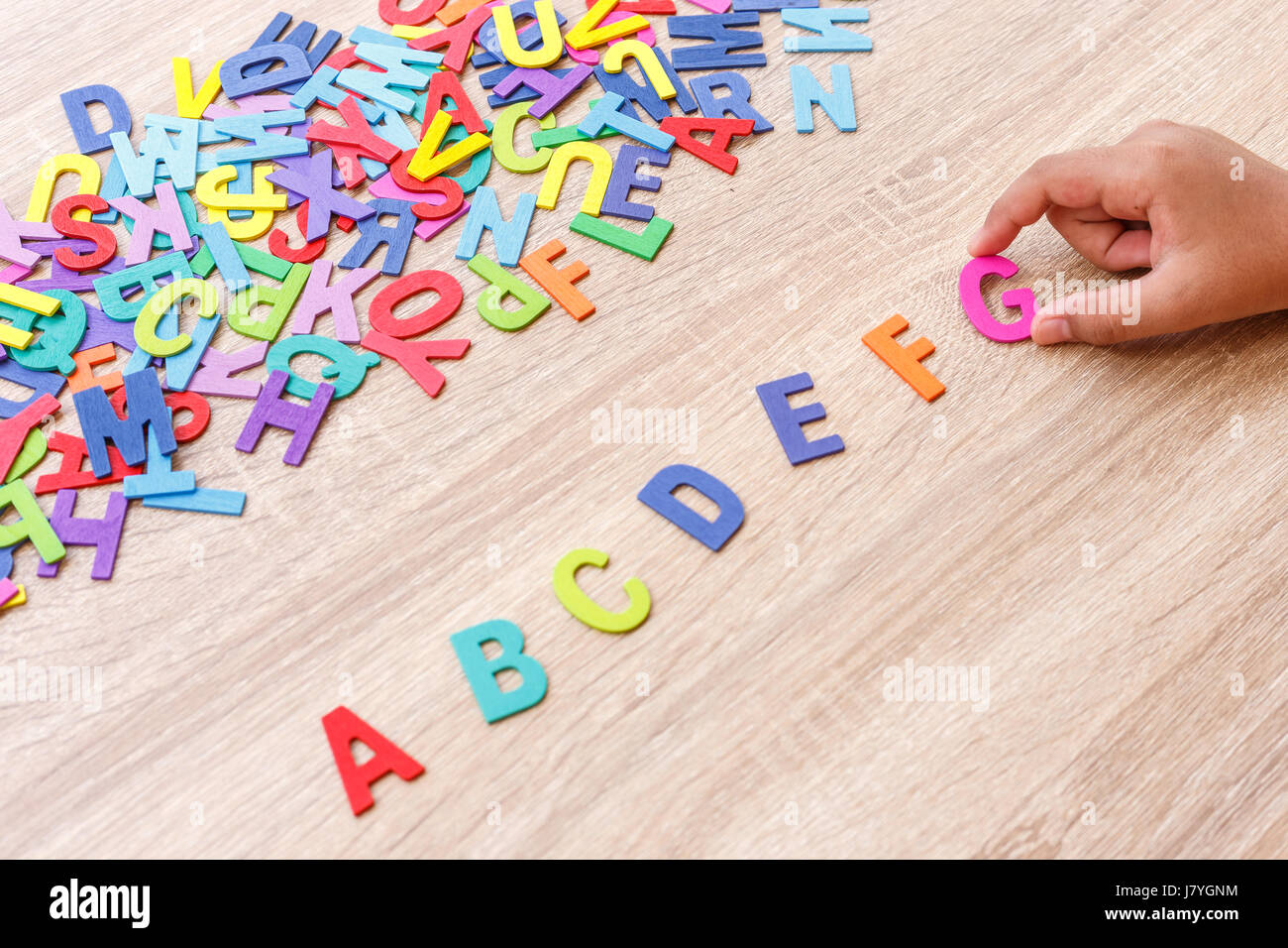 Colorful wooden alphabet and hand sort on G. Top view on grey wooden ...