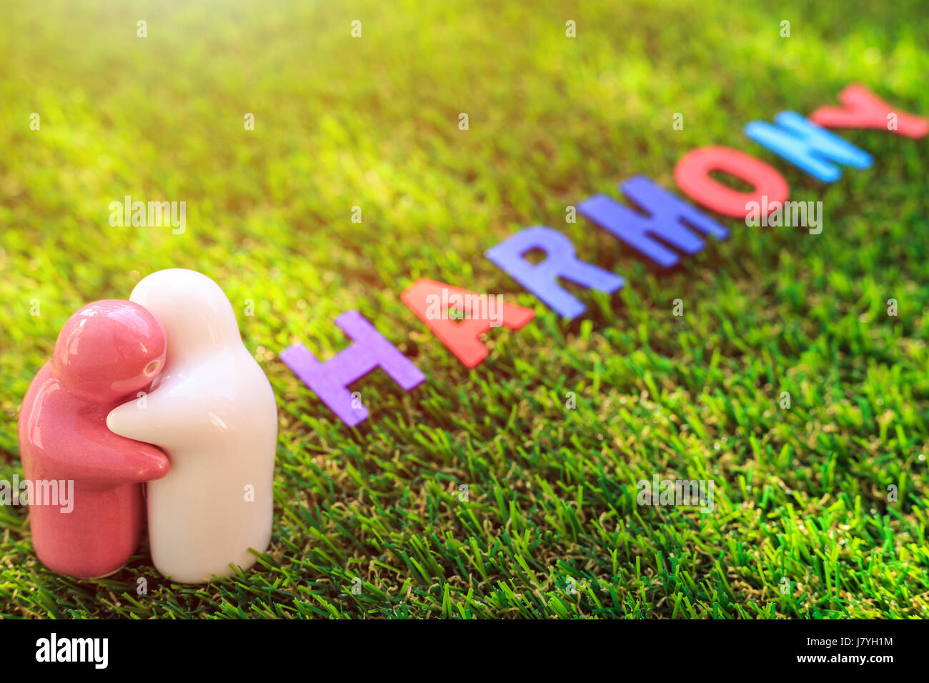 White and pink ceramic doll on green grass with wood text "HARMONY ...