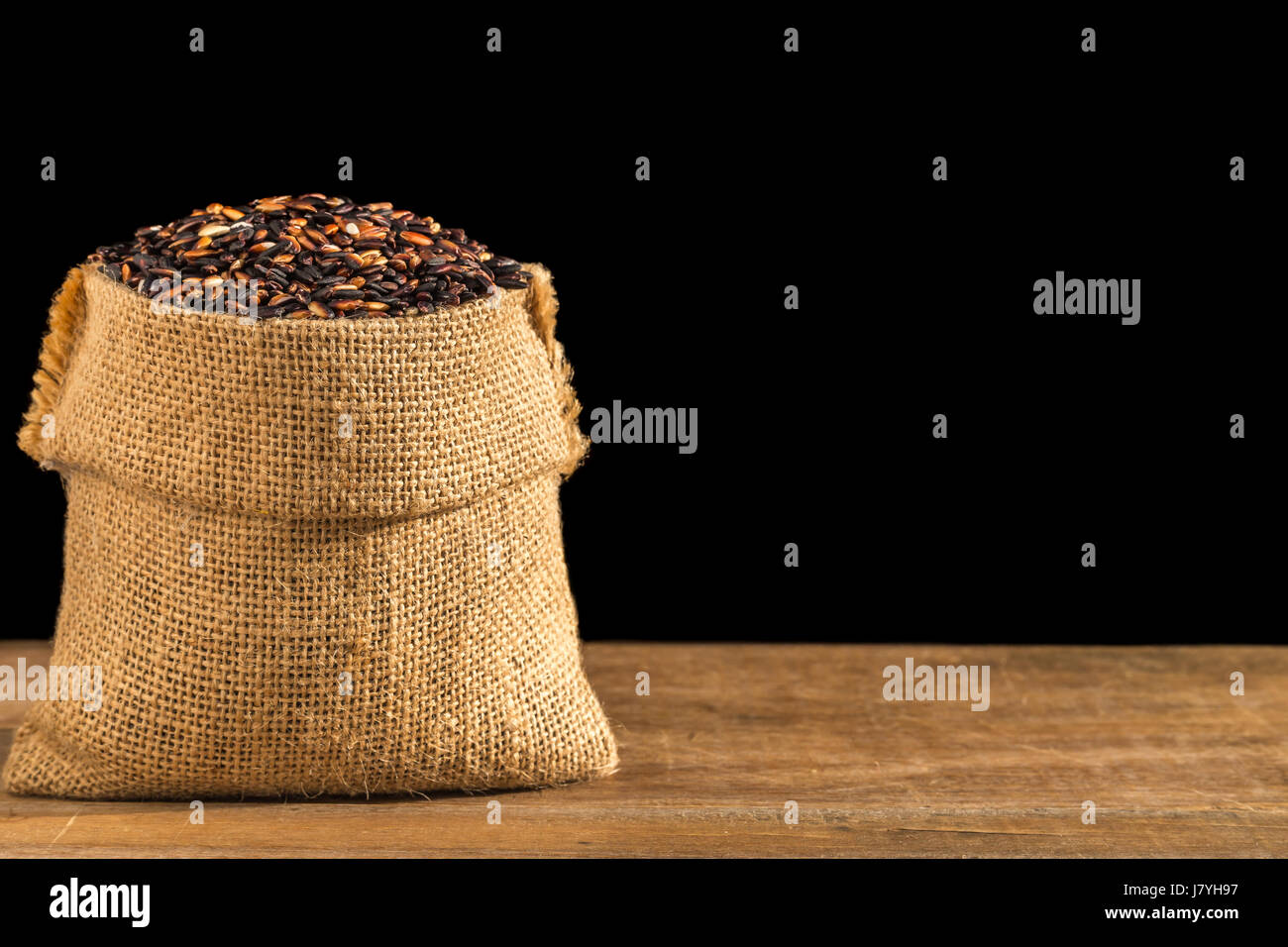 Close up Thai black sticky rice in small sack on wooden table. Isolated ...