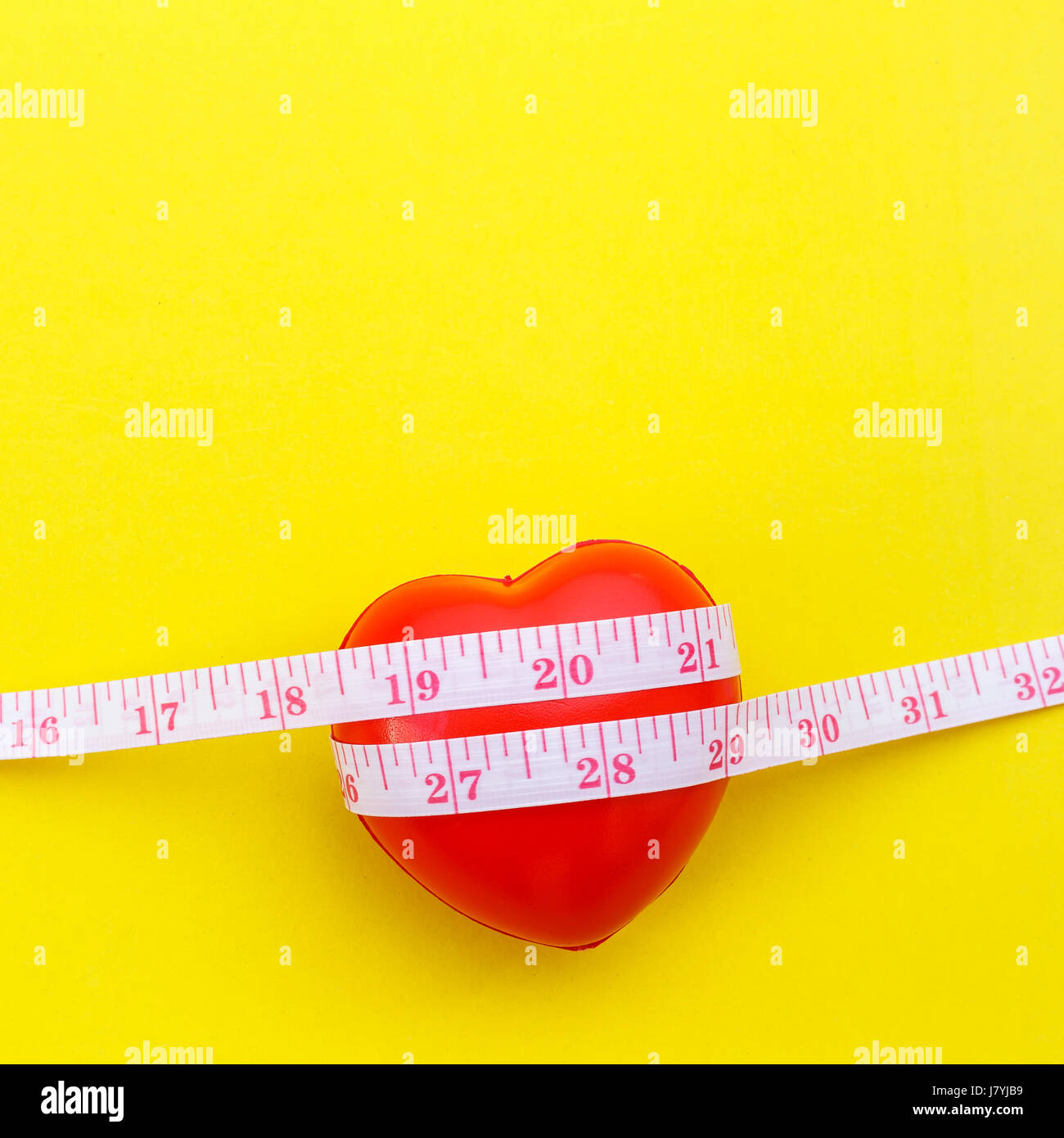 Top view red heart shape and white measurement tape on yellow ...