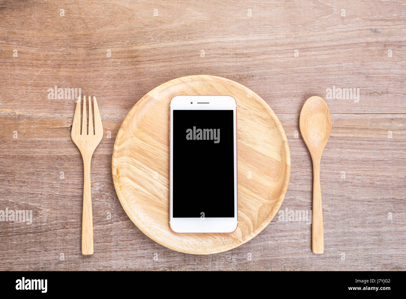 Top view smartphone in wooden dish, spoon and fork on wooden plank ...