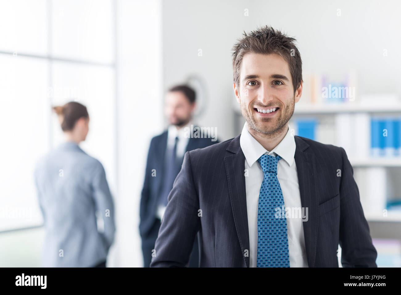 Confident young executive posing in his office, business team in the ...