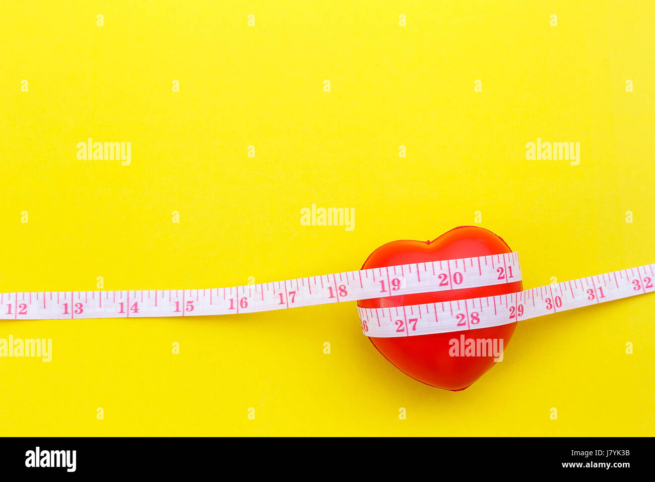 Top view red heart shape and white measurement tape on yellow ...