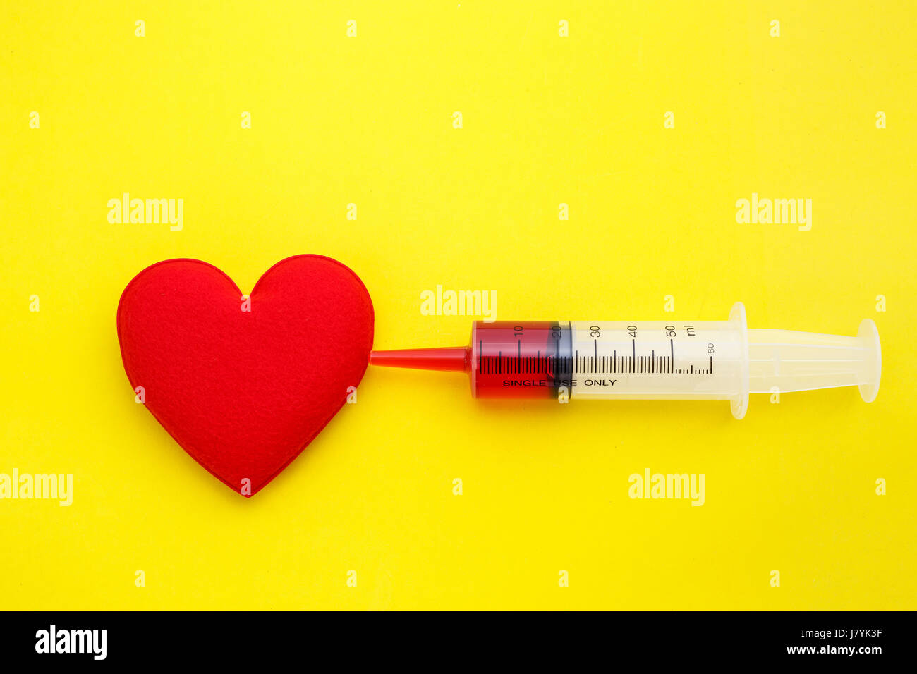 Top view syringe give medicine to red heart shape on yellow background ...