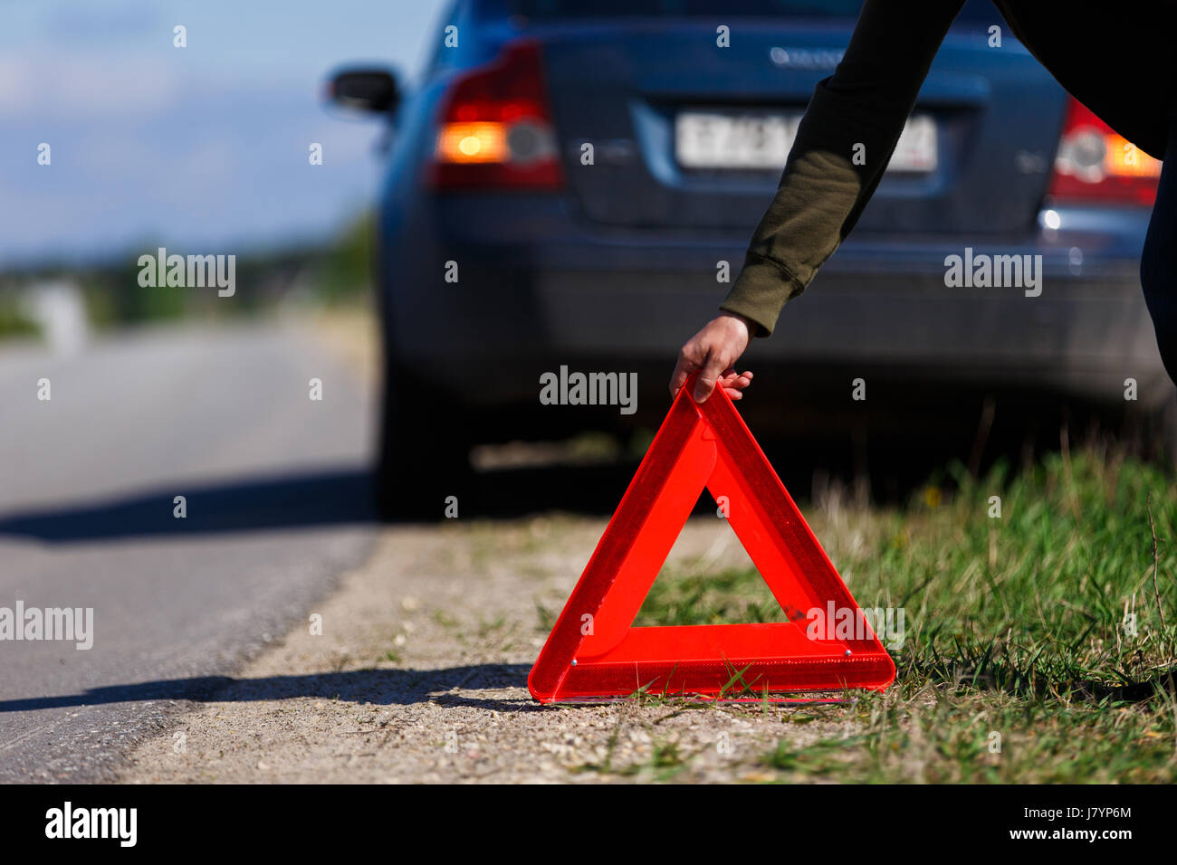 Driver puts red warning triangle on road against background of car ...