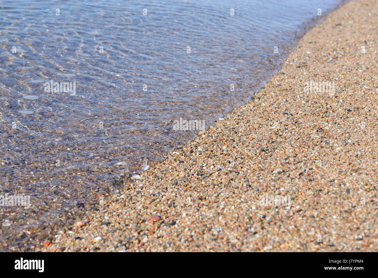 Bright stone sand on the beach and crystal clean sea water in sunny day ...