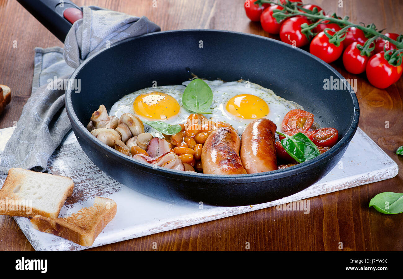 English breakfast in pan with fried eggs, sausages, bacon, beans ...