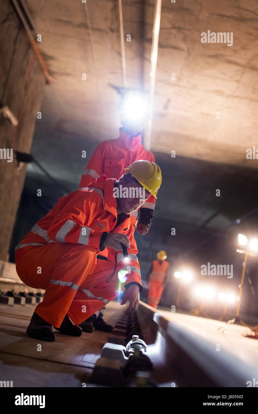 Male construction workers examining underground tracks at dark ...