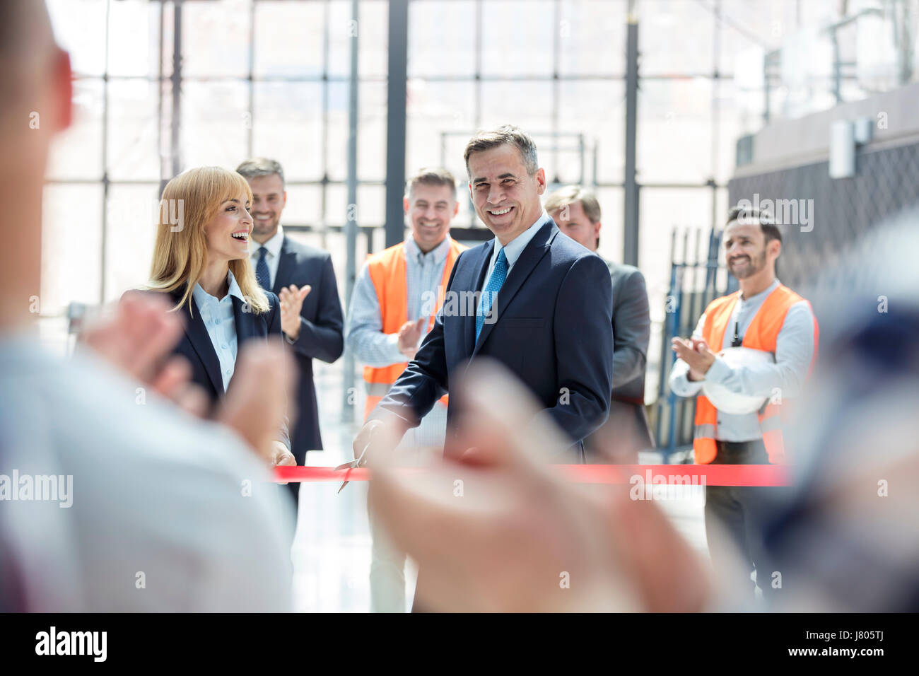 Smiling businessman and businesswoman cutting ribbon at new ...