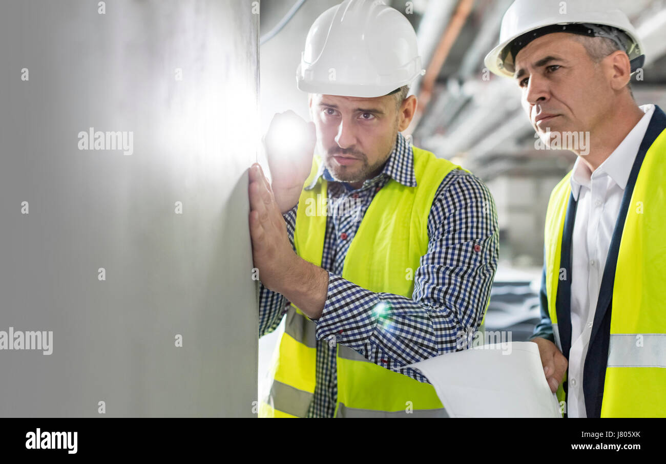 Male engineer with flashlight examining underground wall at ...