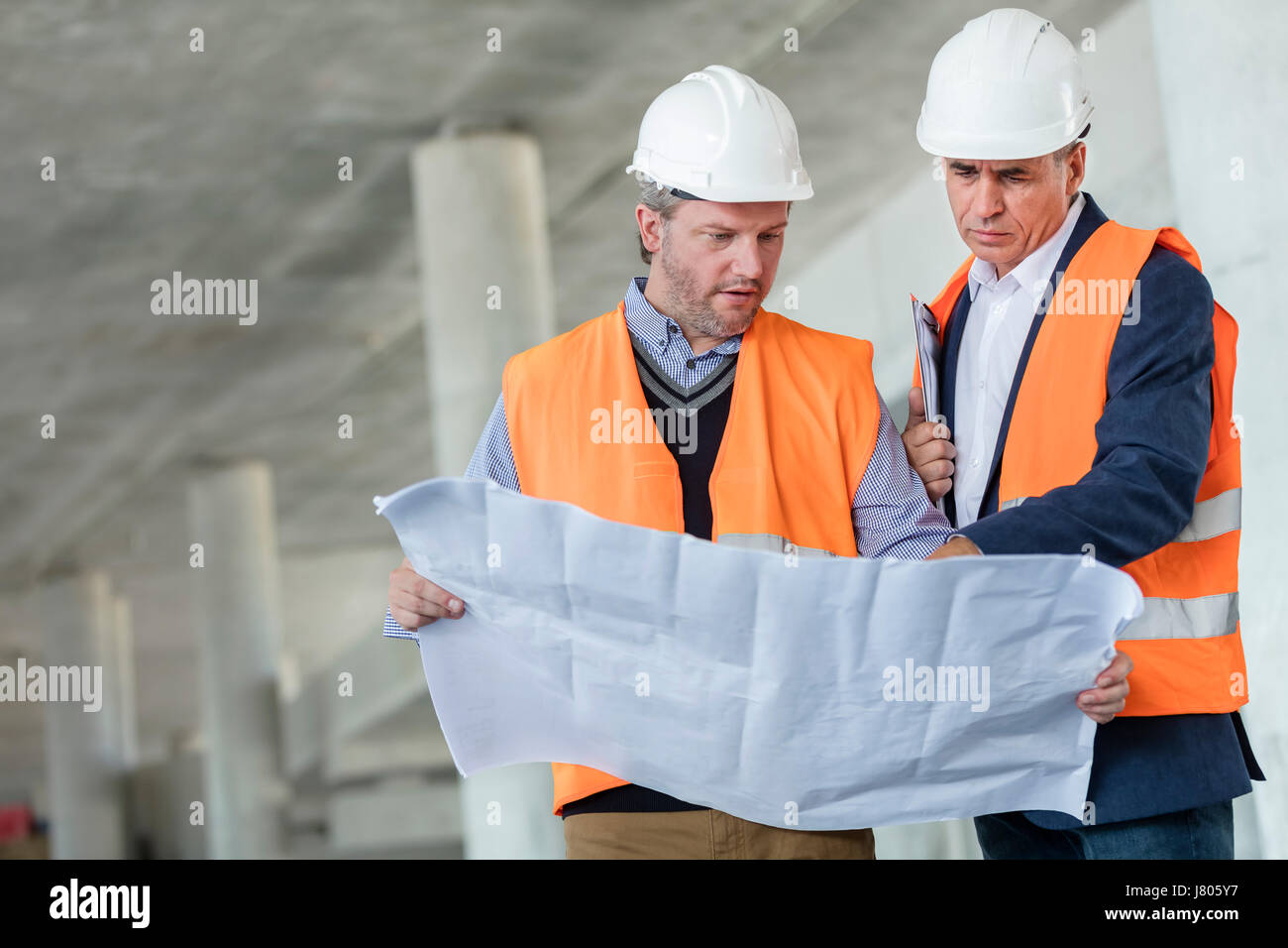 Male engineers examining underground blueprints at construction site ...