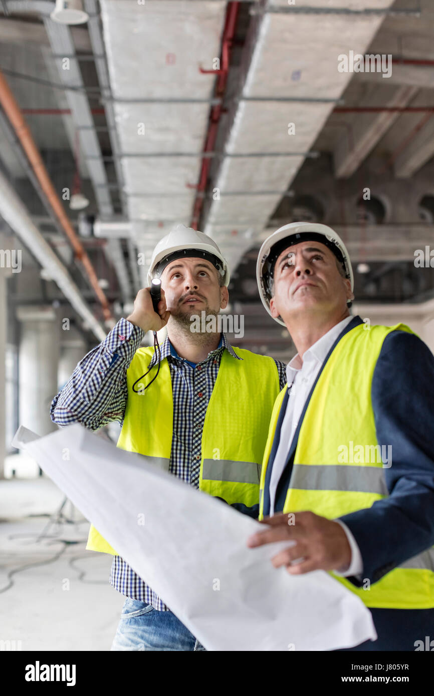 Male engineers with flashlight and blueprints looking up at ...
