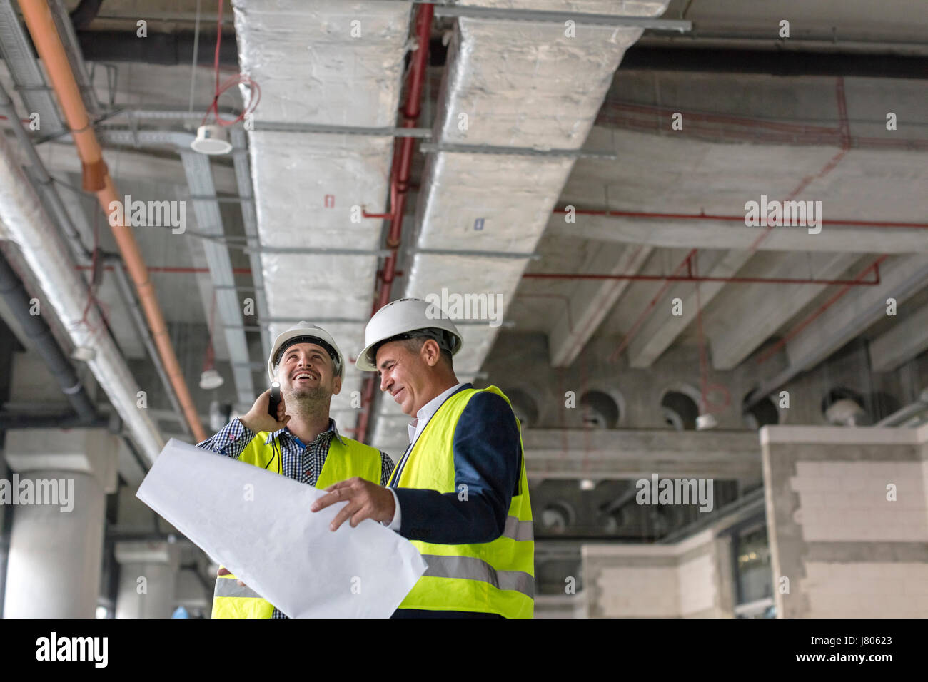 Male engineers with flashlight and blueprints at construction site ...