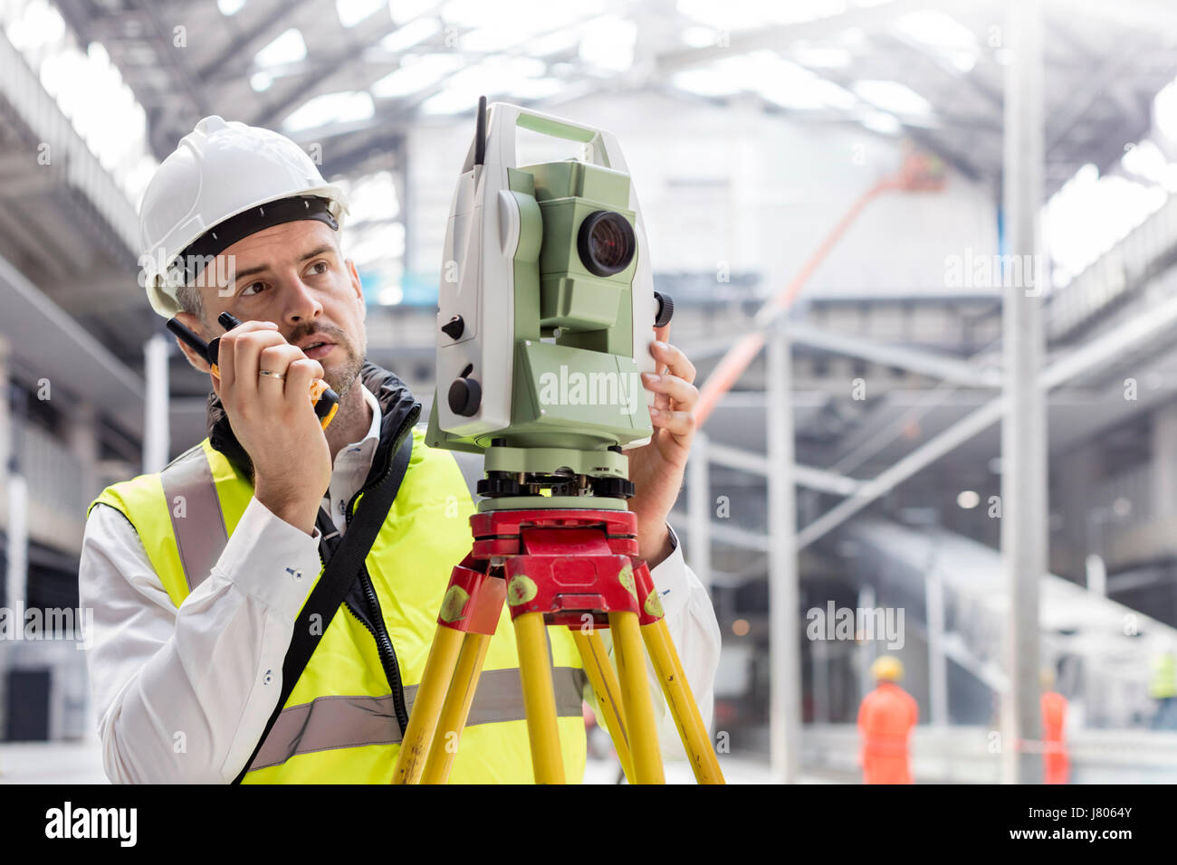 Male engineer using walkie-talkie and theodolite at construction site ...