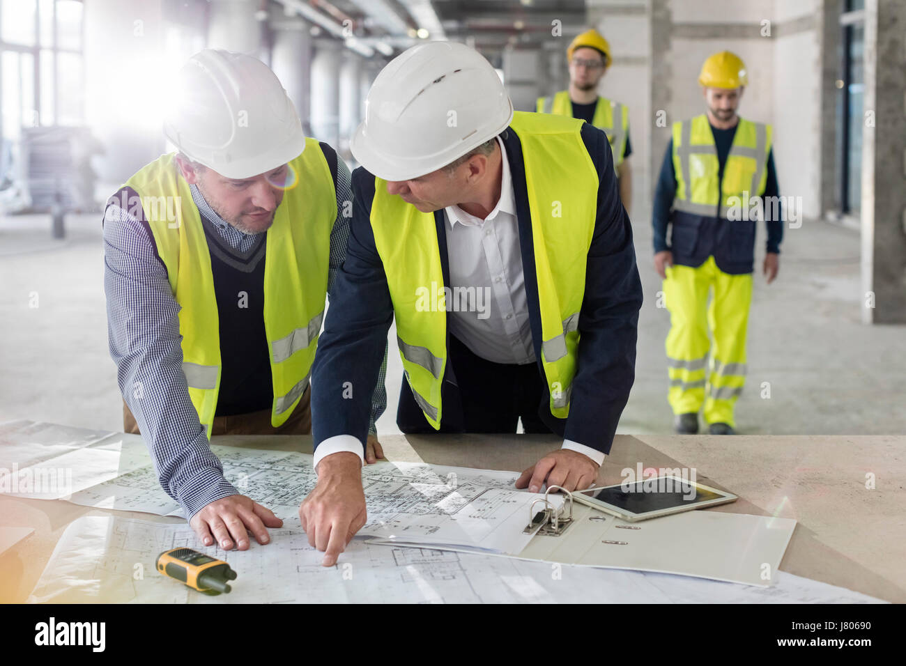 Male engineers discussing blueprints at construction site Stock Photo ...