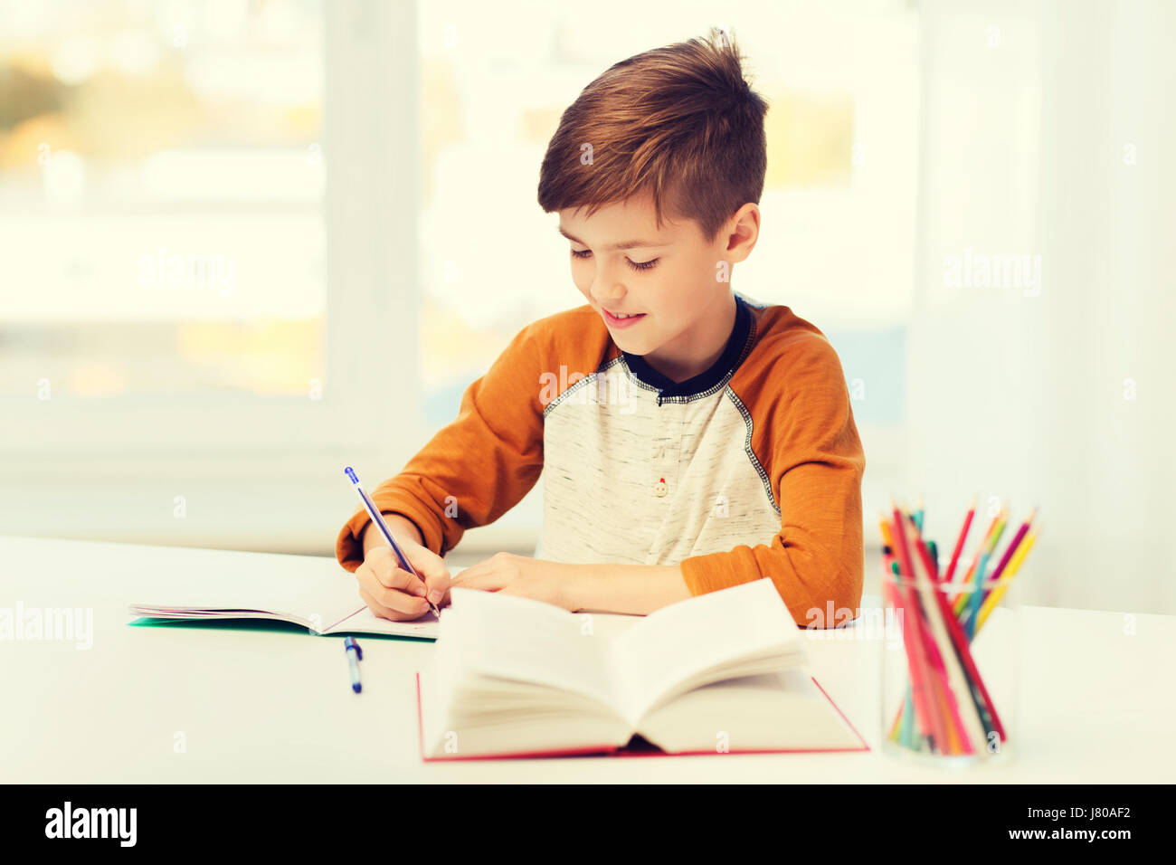 smiling student boy writing to notebook at home Stock Photo - Alamy