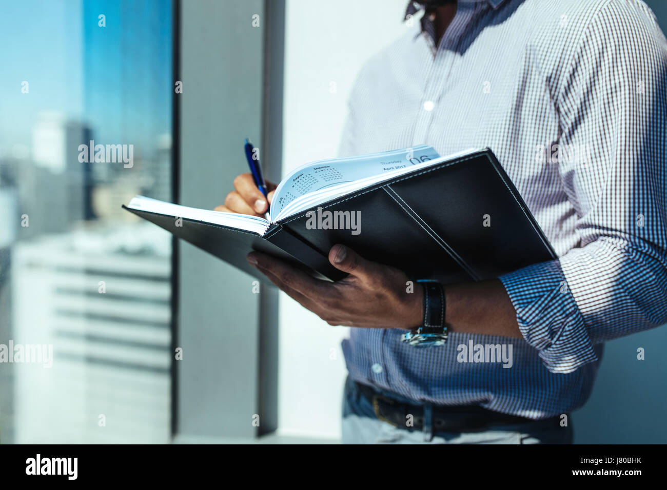 Businessman holding an open diary standing beside a window in office ...