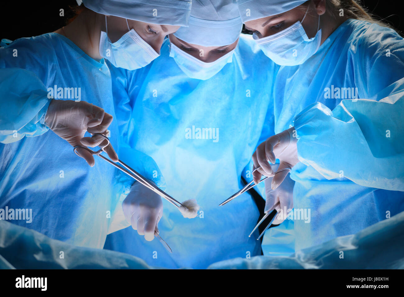 Group of surgeons at work in operating theater toned in blue. Medical ...