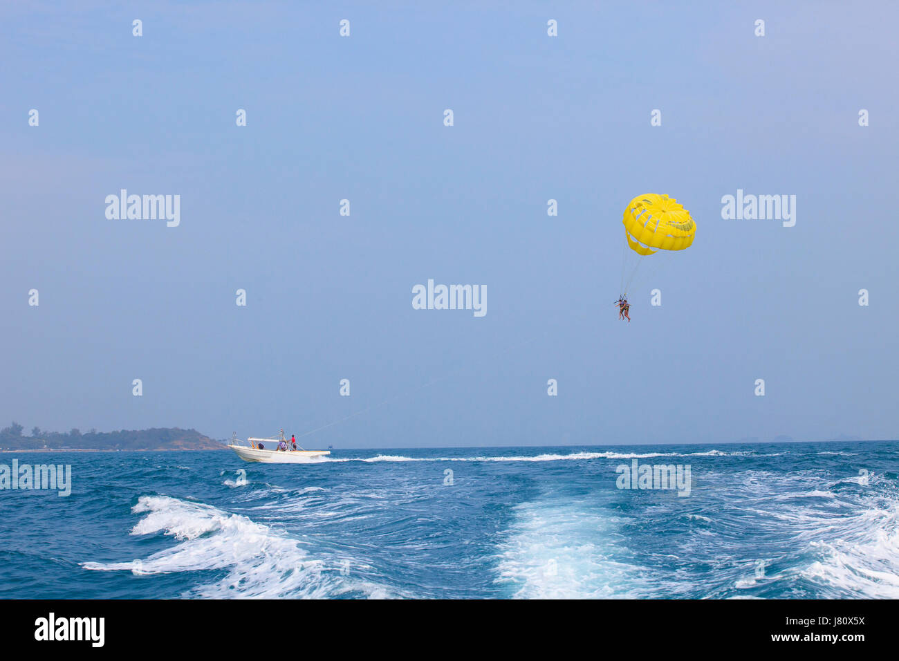 two of young people playing parashoot umbrella by boat pulling in sea ...