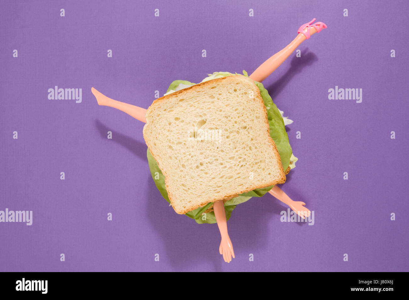 Parts of a doll's body in a sandwich with salad and soft bread on a ...