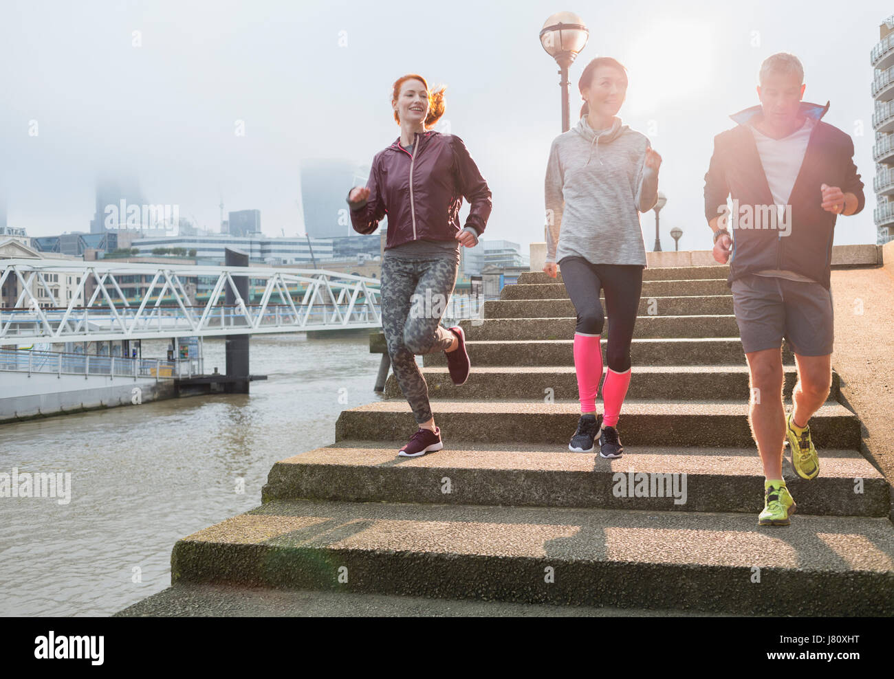 Runners running down steps along sunny urban waterfront Stock Photo - Alamy