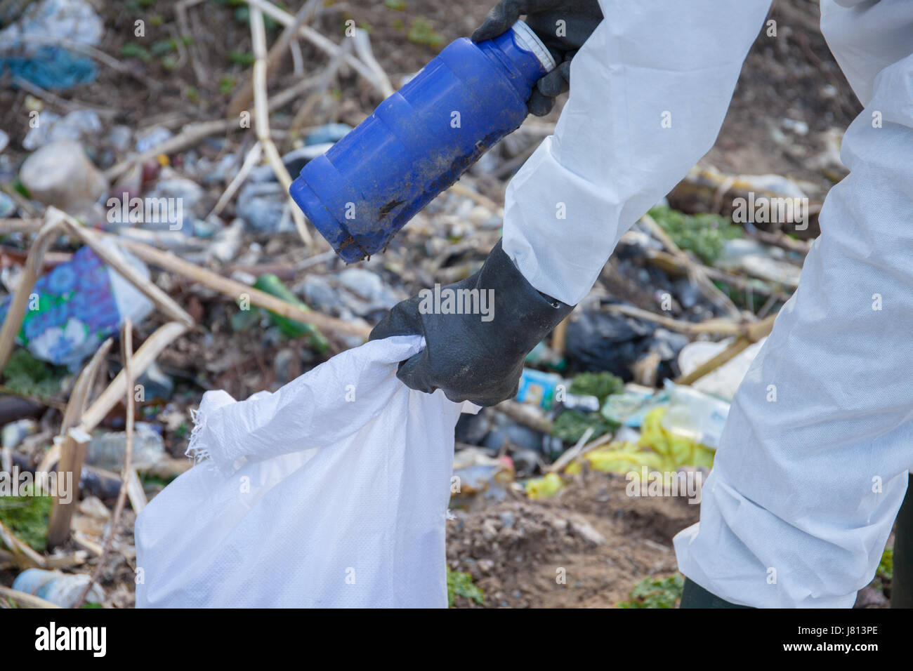 A volunteer man in white protective clothing collects garbage. Hand ...