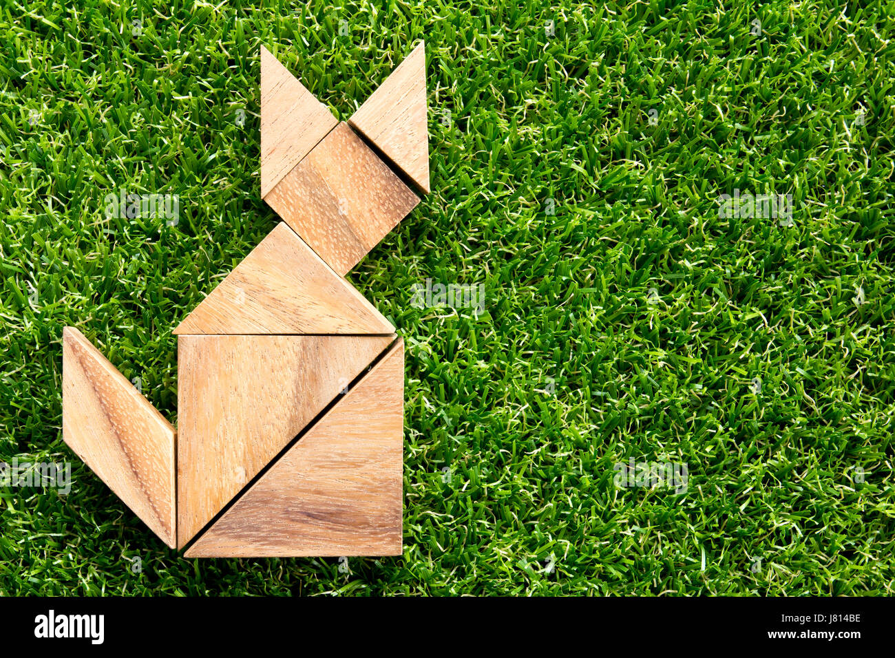 Wooden tangram puzzle in cat shape on artificial green grass background ...