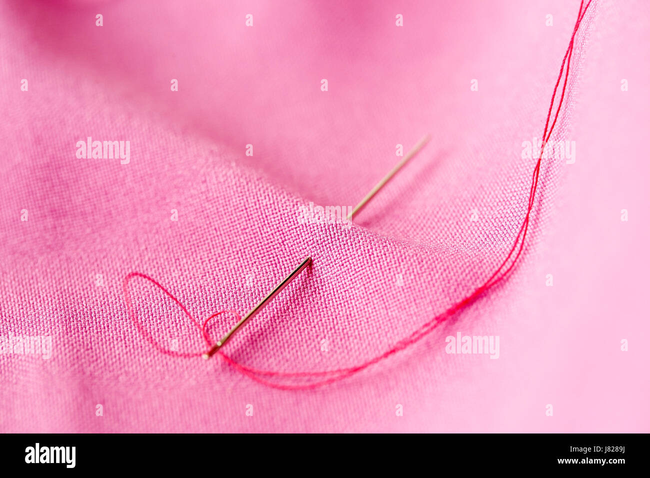 sewing needle with thread stuck into pink fabric Stock Photo - Alamy