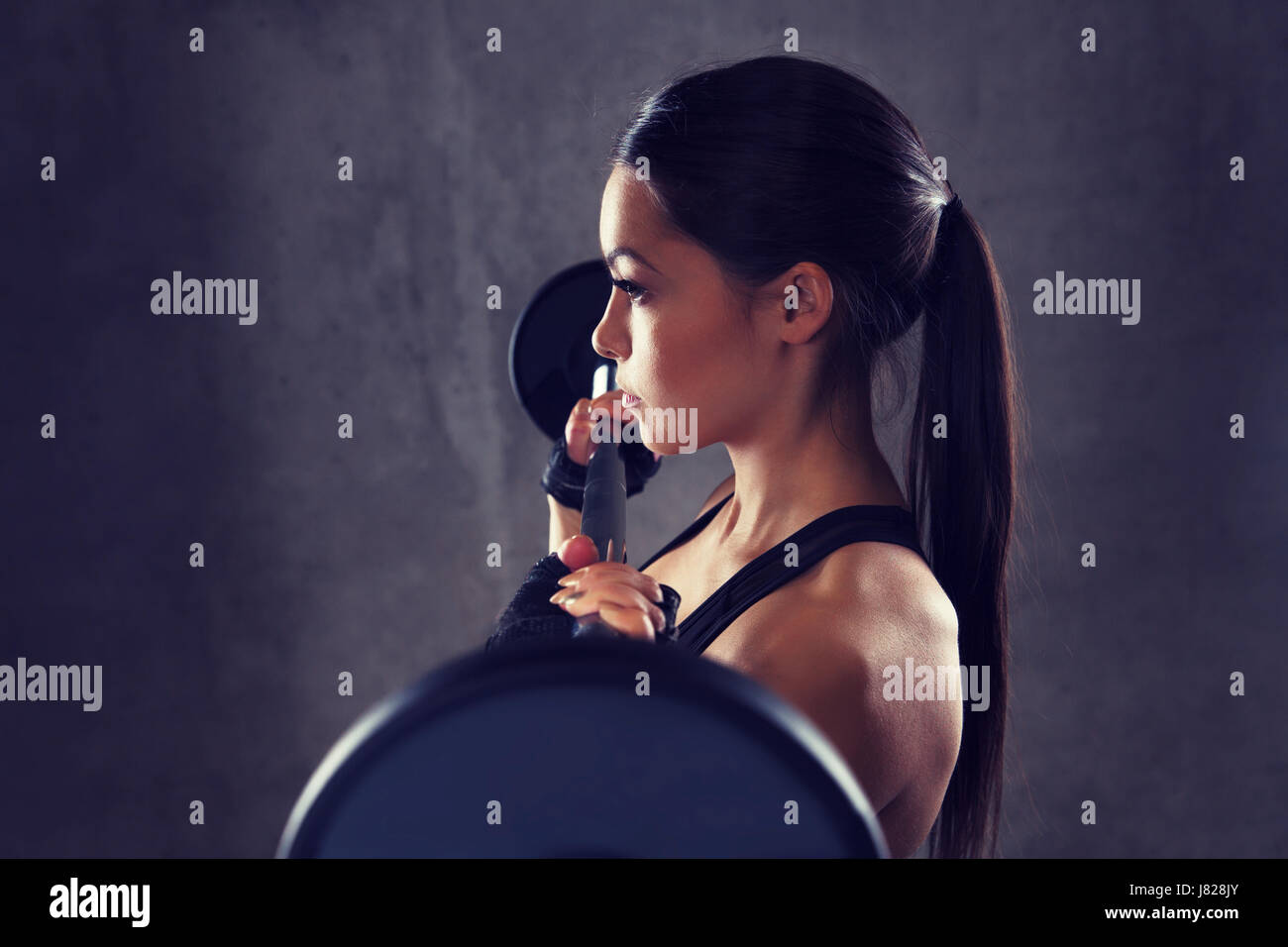 young woman flexing muscles with barbell in gym Stock Photo - Alamy