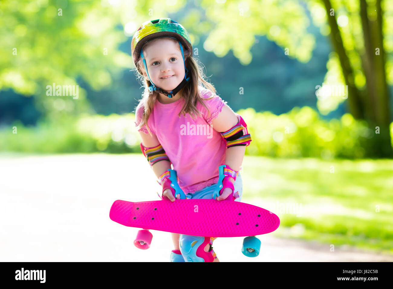 Child riding skateboard in summer park. Little girl learning to ride ...
