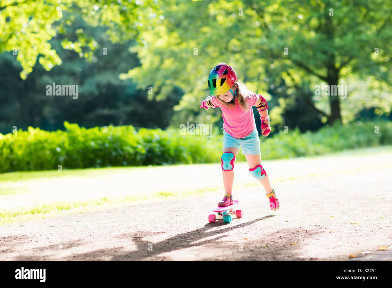 Child riding skateboard in summer park. Little girl learning to ride ...