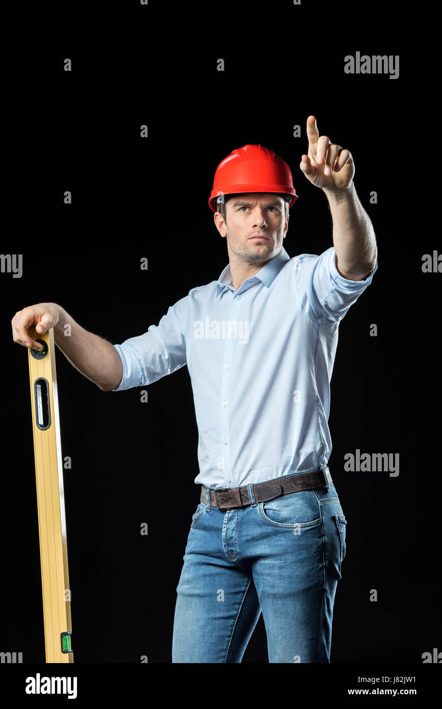 Male engineer in hard hat holding level tool and pointing with finger ...