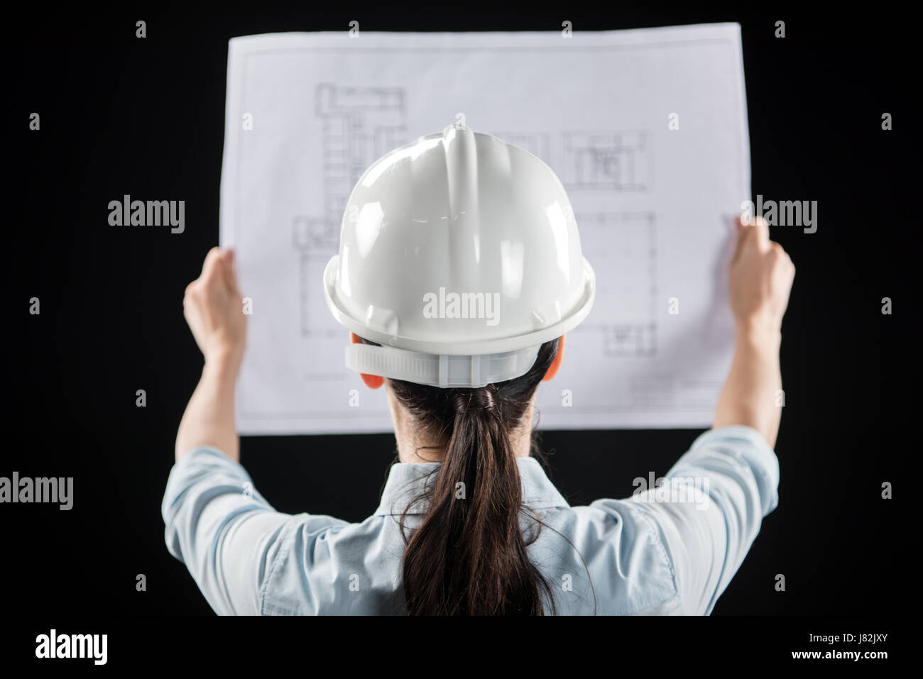Back view of female architect in white helmet looking at blueprint ...