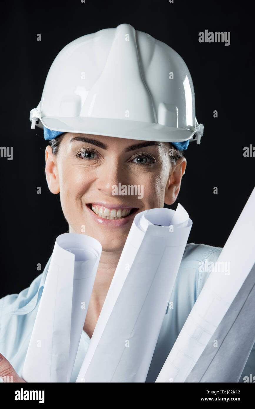 Smiling female architect in helmet holding blueprints and looking at camera Stock Photo - Alamy