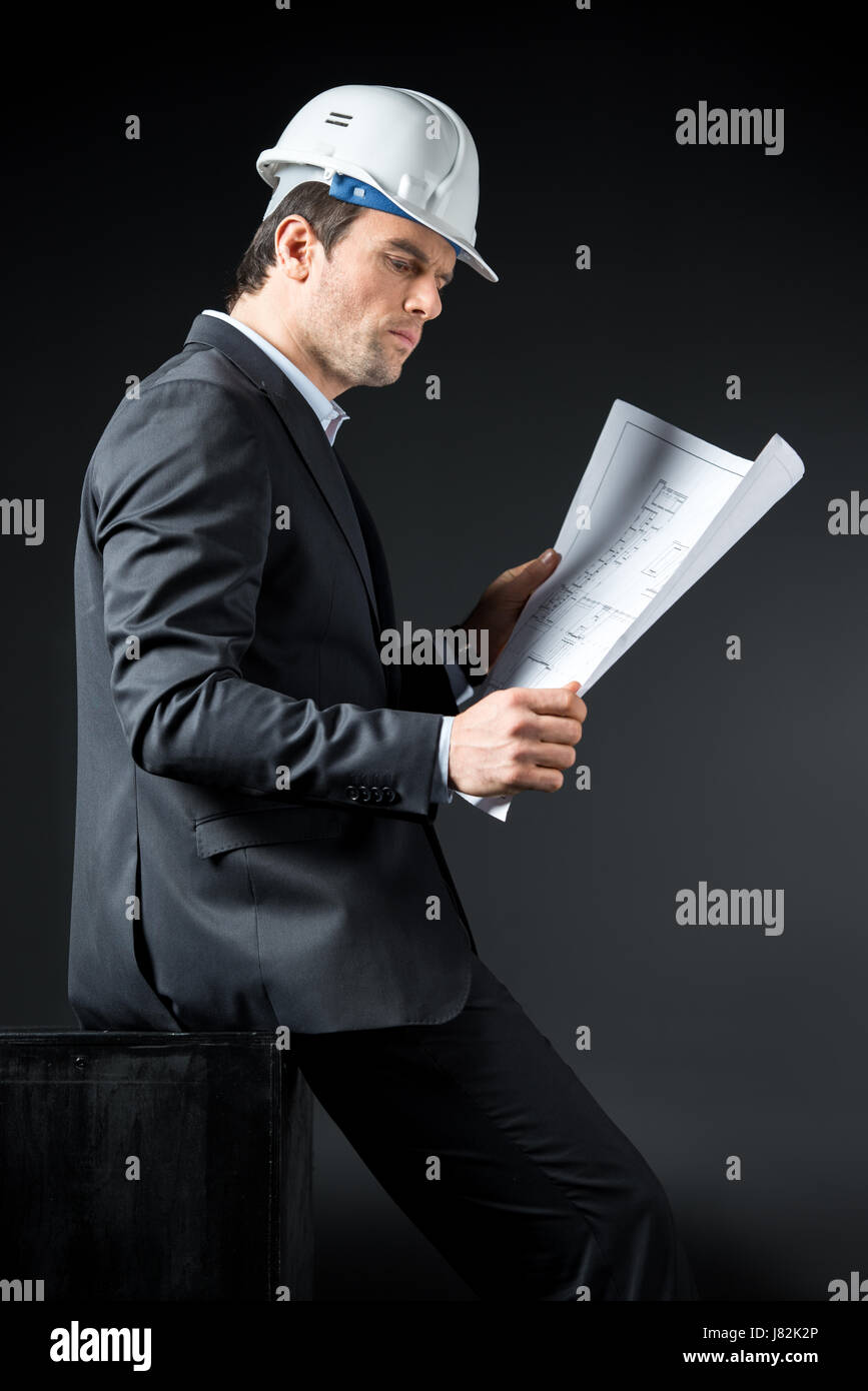Attentive male engineer in helmet looking at blueprint on black Stock ...