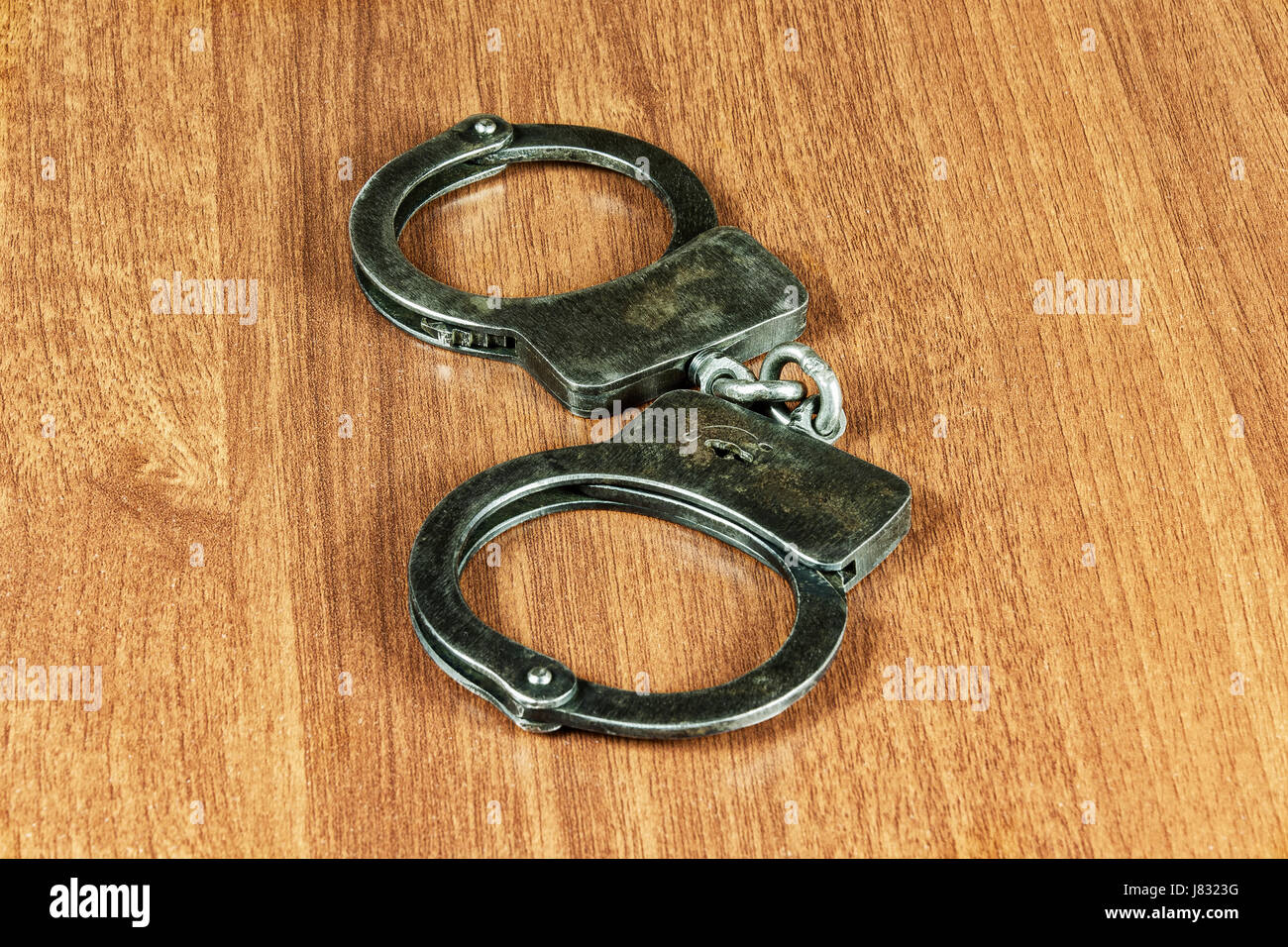 Metal handcuffs lie on a wooden table Stock Photo - Alamy