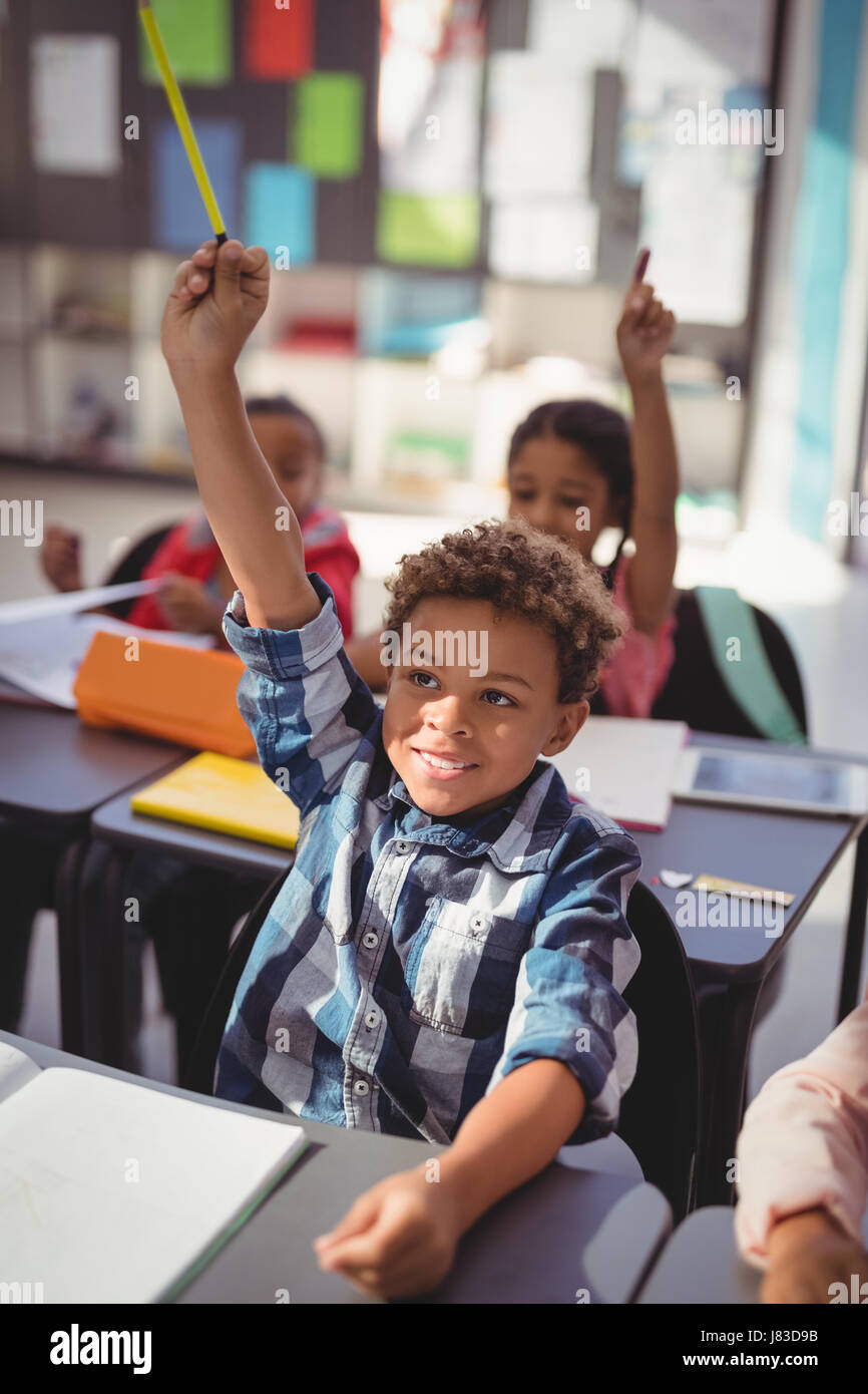 Schoolkids raising their hands in classroom at school Stock Photo - Alamy