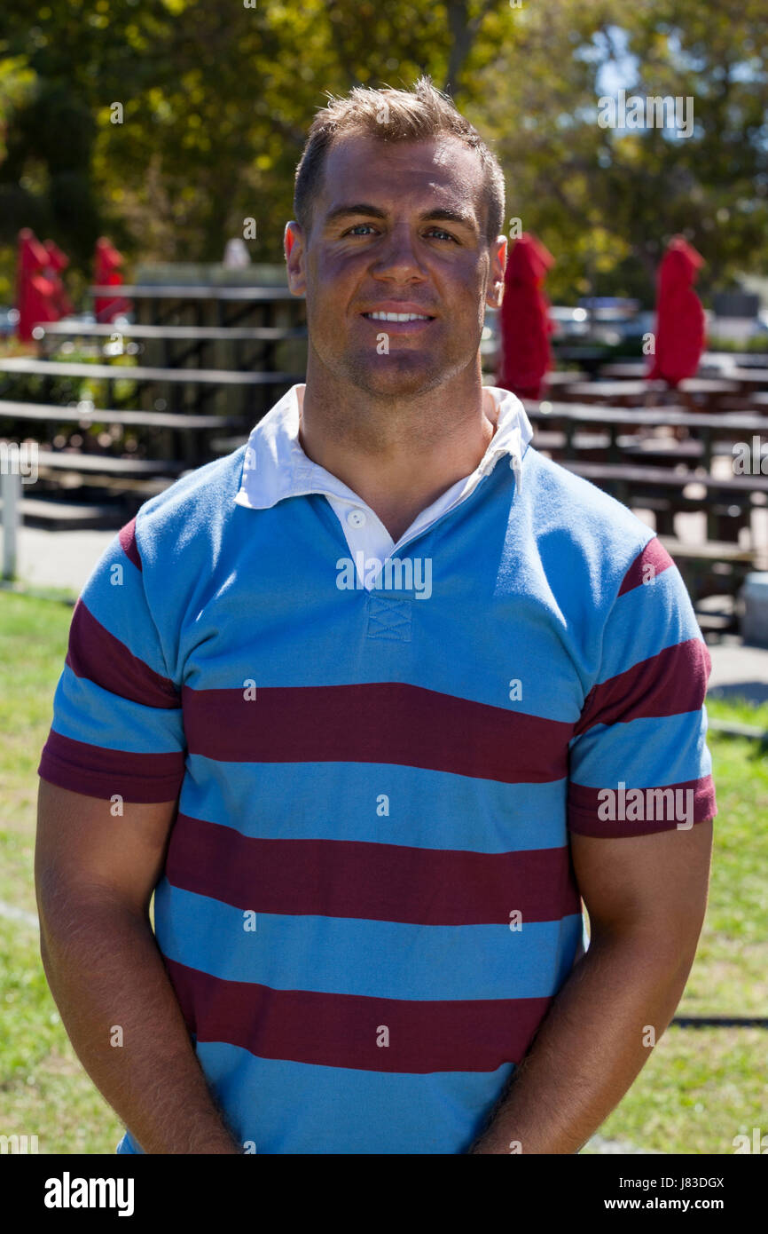 Portrait of smiling rugby player standing at playing field on sunny day ...